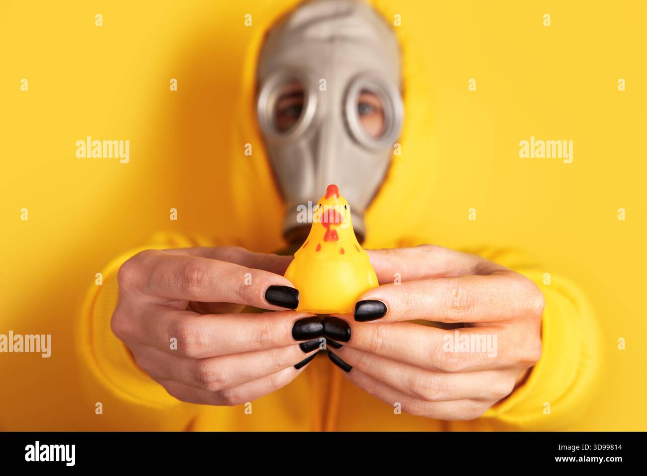 Individual in gas mask and yellow hoodie holds rubber chicken toy ...