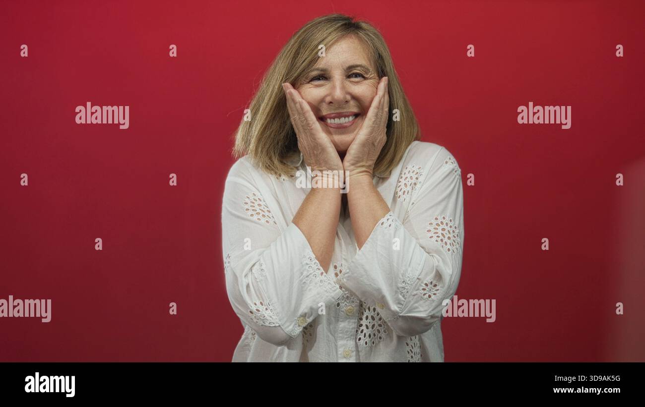 Middle aged caucasian woman with smiling face covers cheeks with hands ...