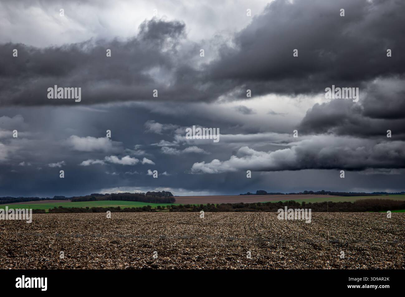 Dramatic storm clouds gathering over a plowed field and distant ...