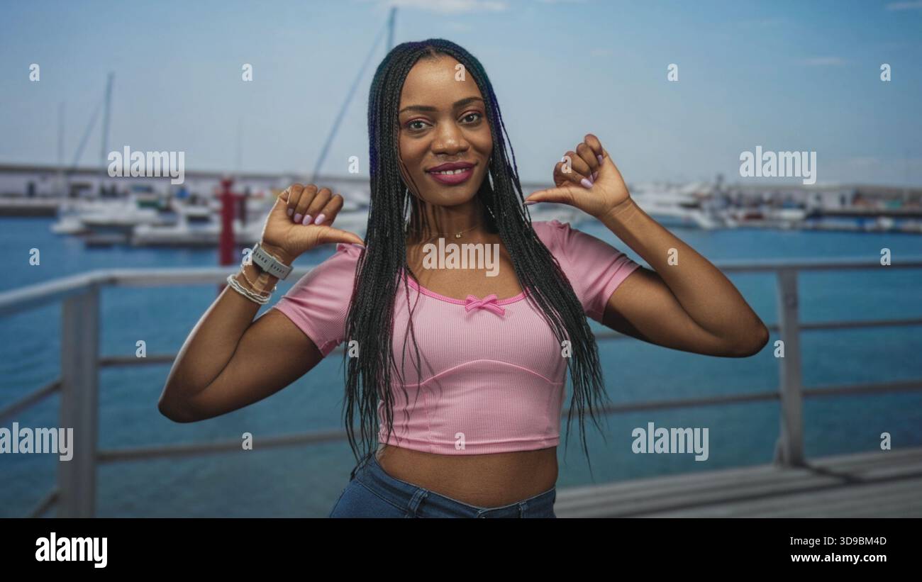 Woman points thumbs to chest showing midriff and smiles wearing pink ...