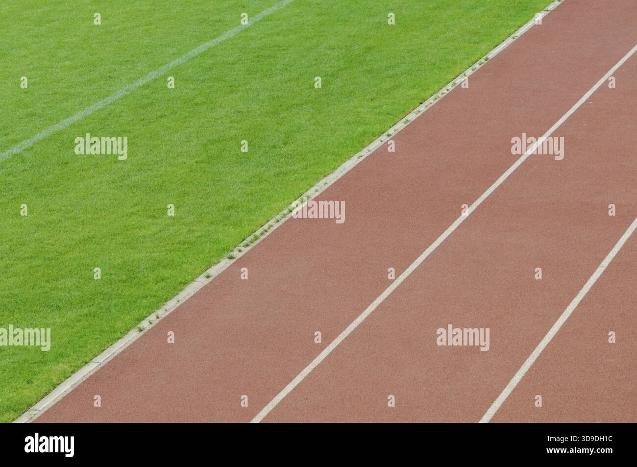 Red running track lines meeting green grass field in stadium, creating ...