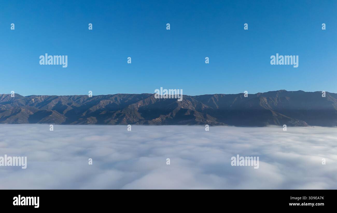 Aerial view of a sea of clouds stretching to meet the base of rugged ...