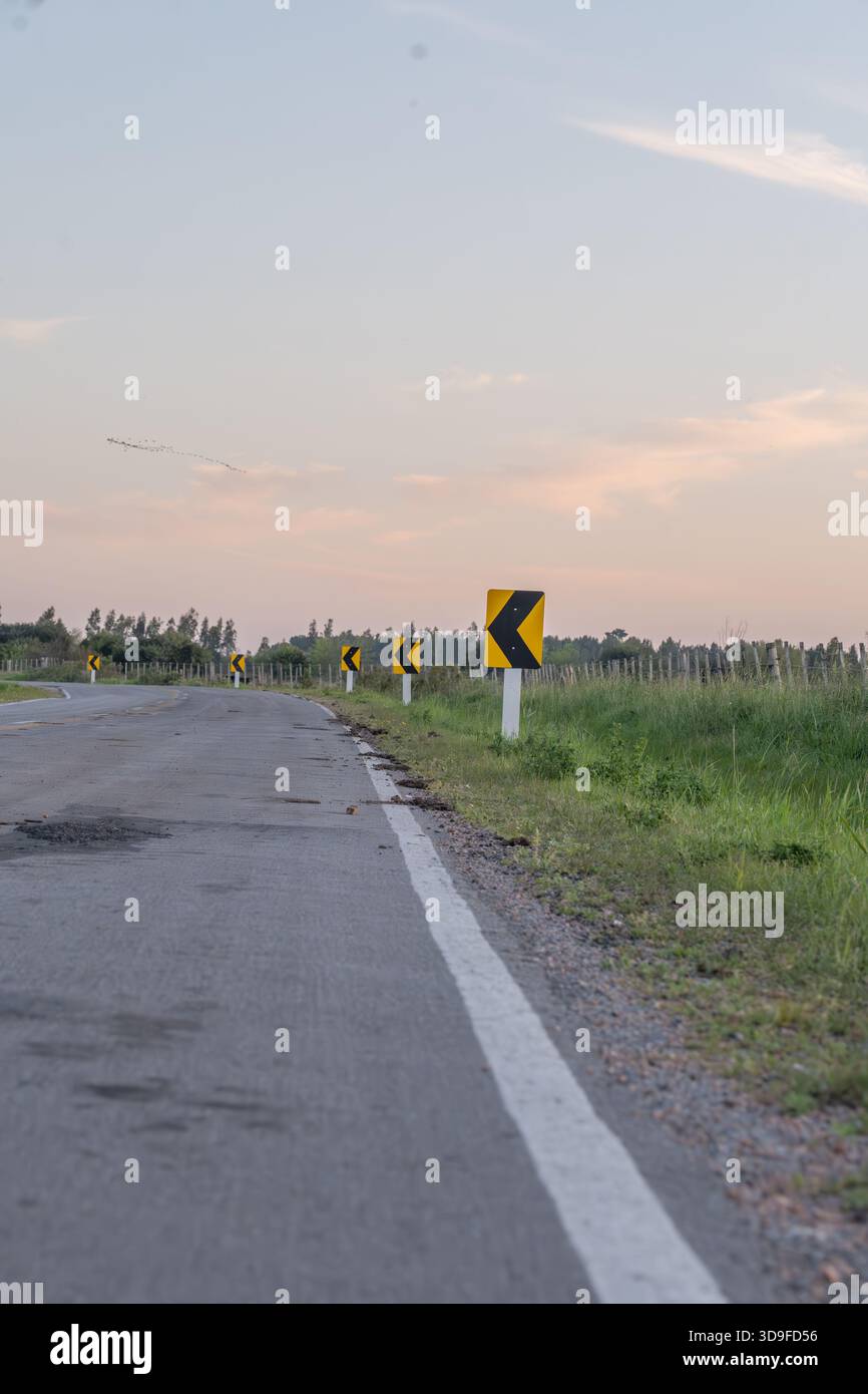 View down a curving asphalt road lined with multiple chevron alignment ...