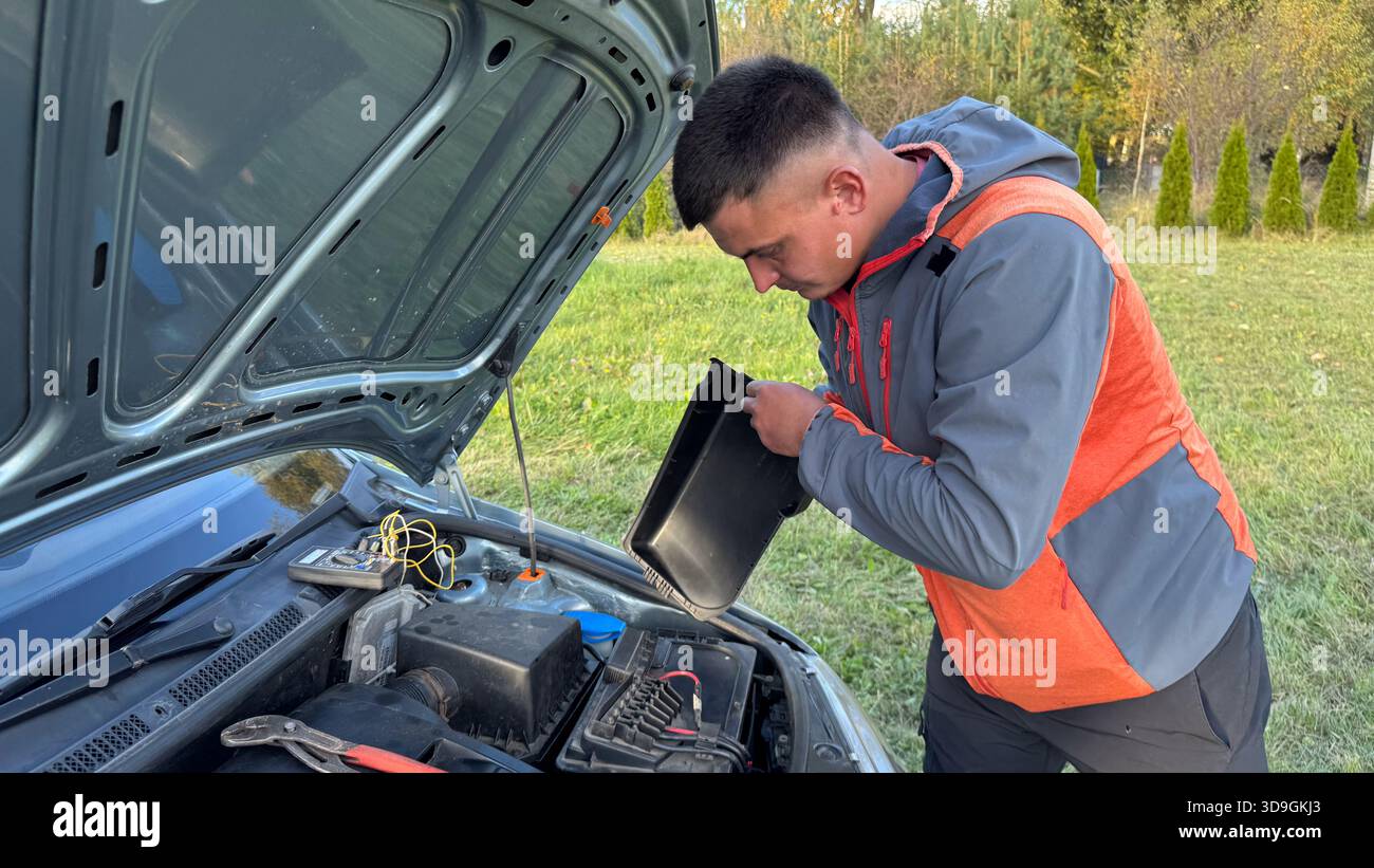 A Caucasian male mechanic in an orange and gray jacket opening the ...
