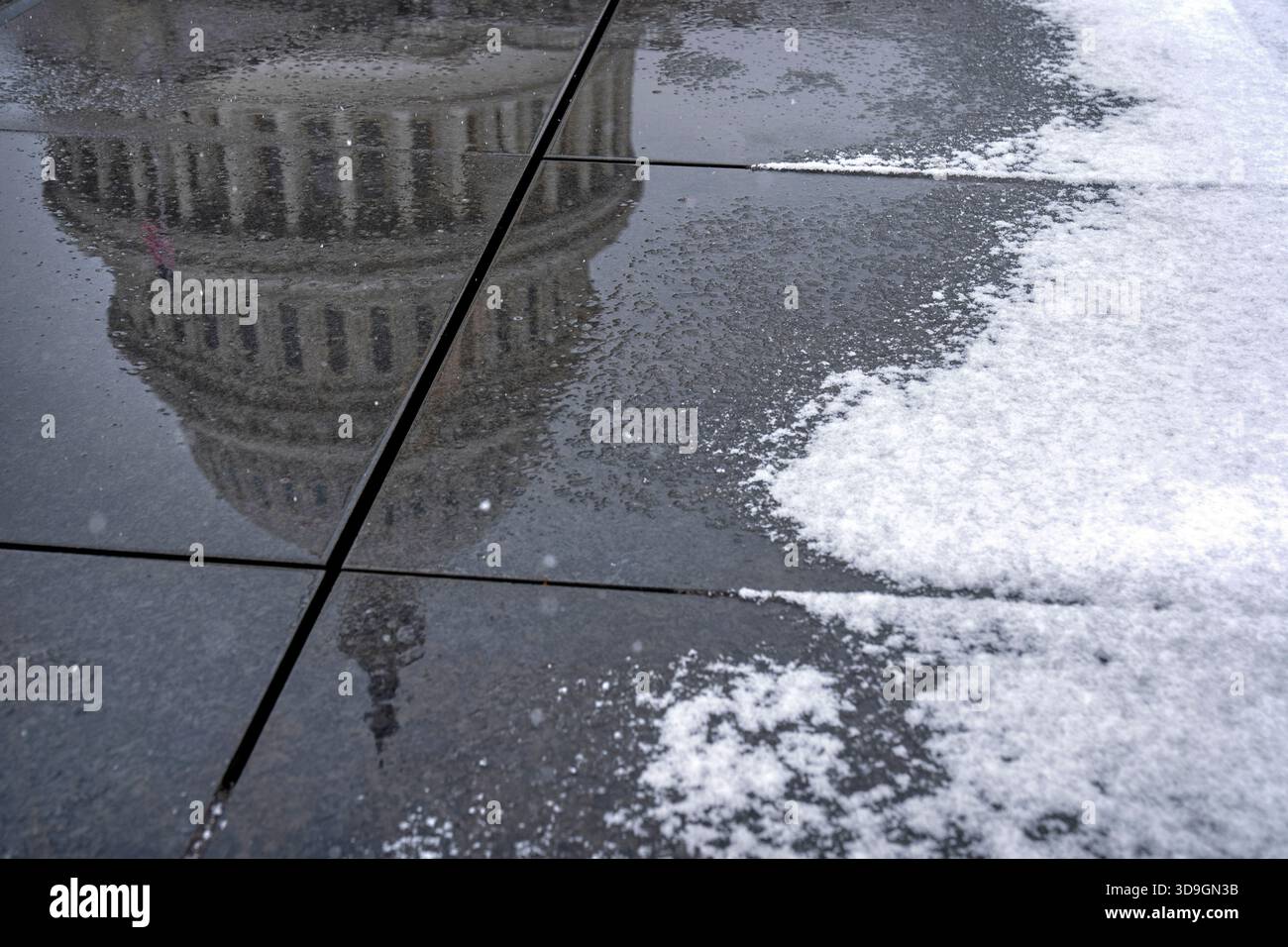 The dome of the Capitol is reflected in a puddle of melted snow during ...