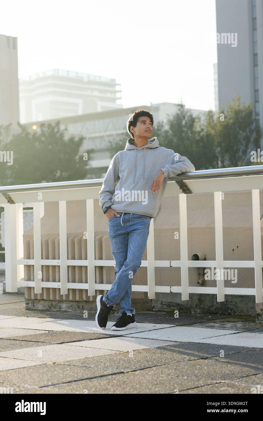 Male in his twenties leaning against white metal rail barrier on tiled ...