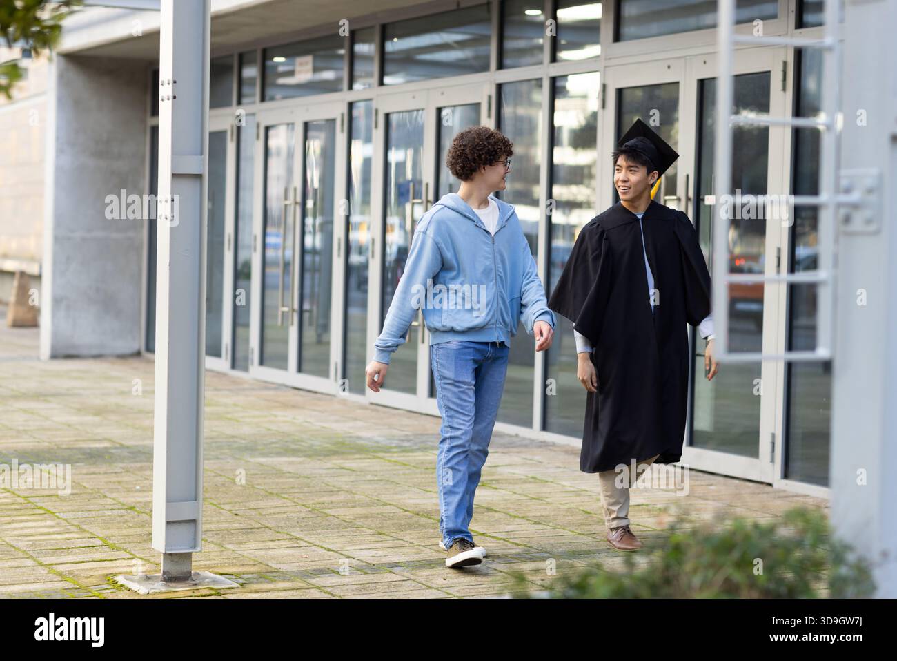 Diverse male students crossing walkway by support post outside glass ...