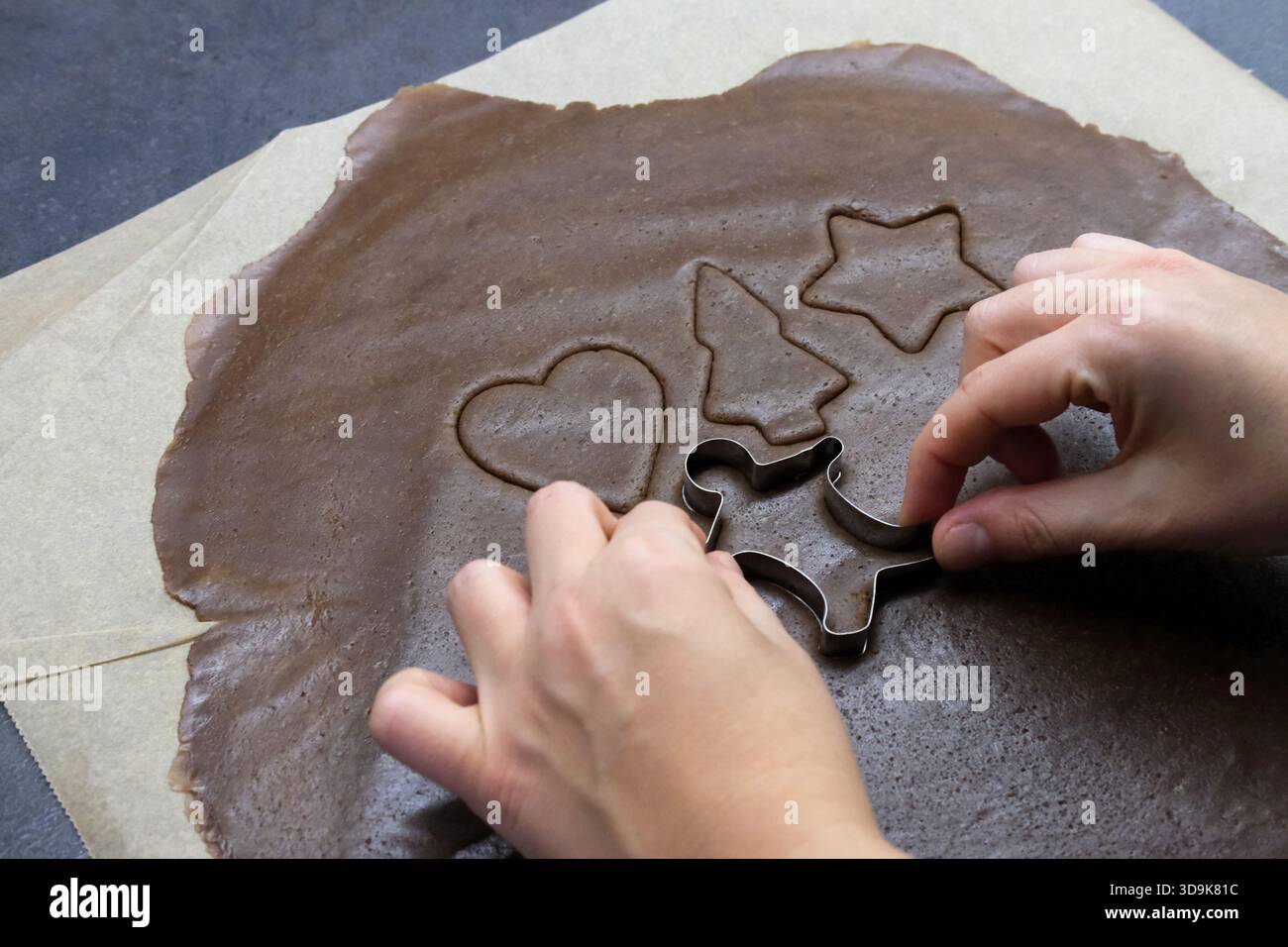 Hands lower gingerbread-man cutter onto rolled brown dough with ...