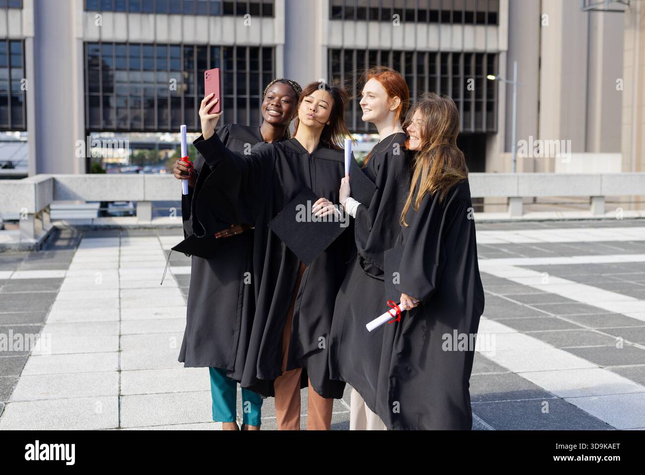 Diverse female graduates taking selfie in campus courtyard with ...