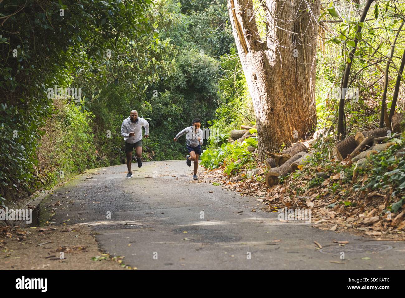 African American father and son running side by side along wooded park ...