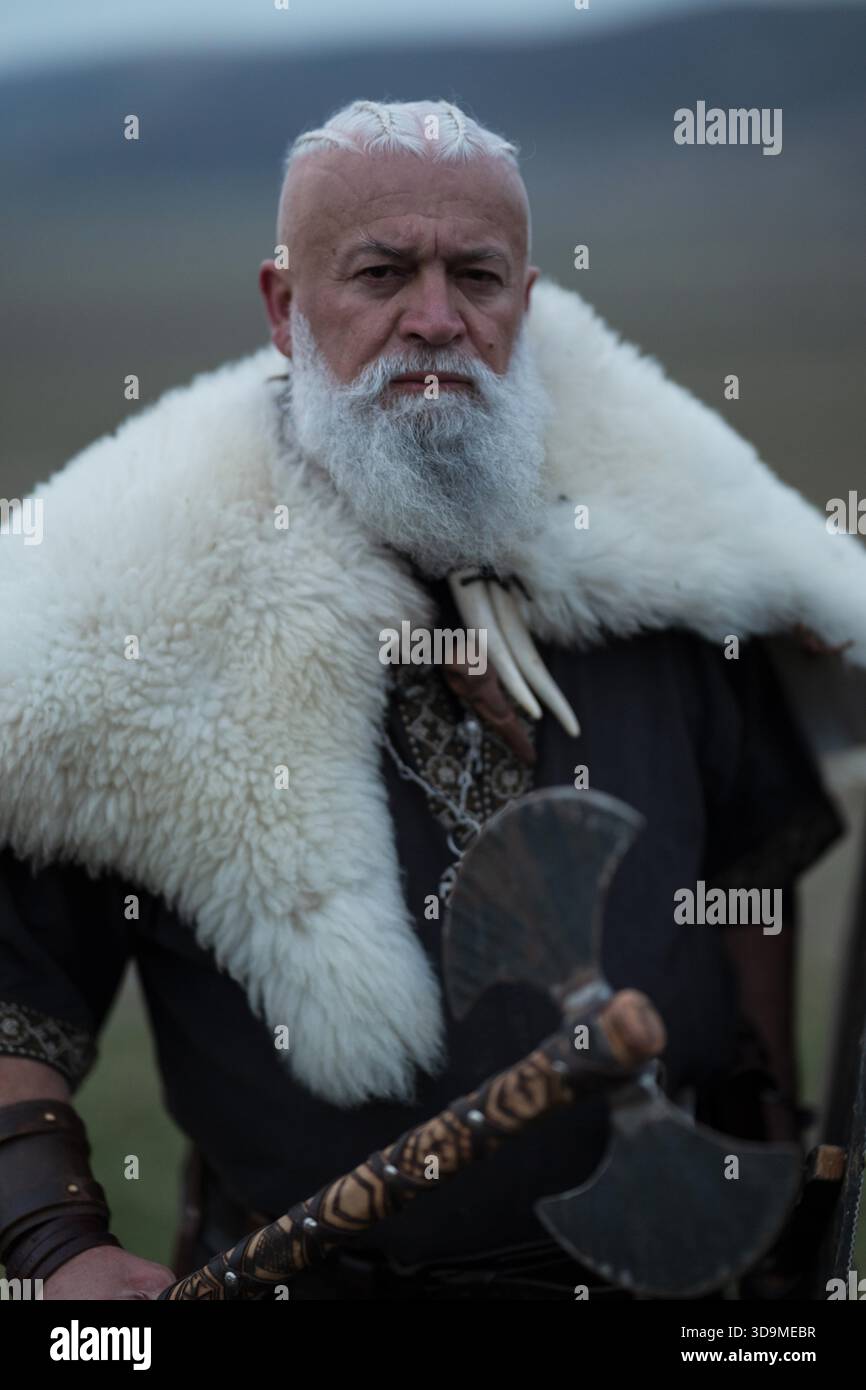 Viking warrior with axe standing on mountain cliff, wearing fur cloak ...