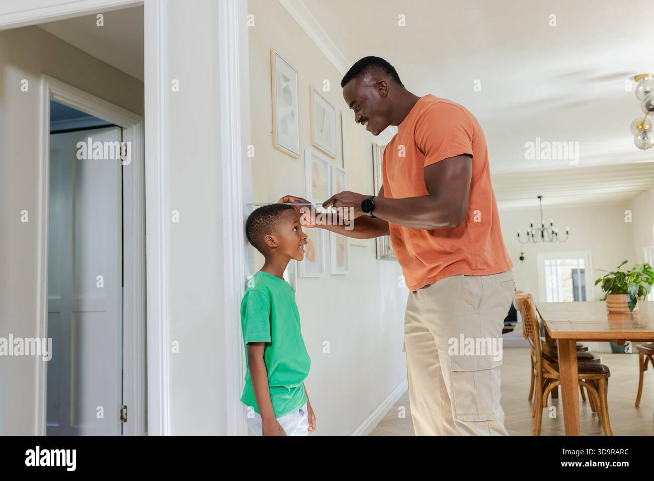 African American father and child measuring height against wall with ...
