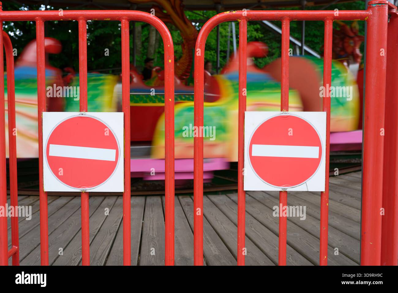 Children carousel is closed off by a red metal gate. Two warning signs ...