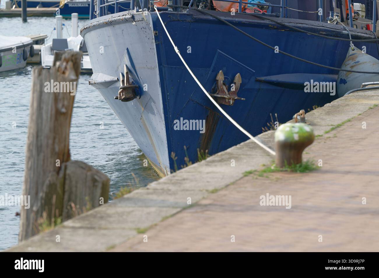 A blue metal ship is docked at the port, tied with thick ropes to shore ...