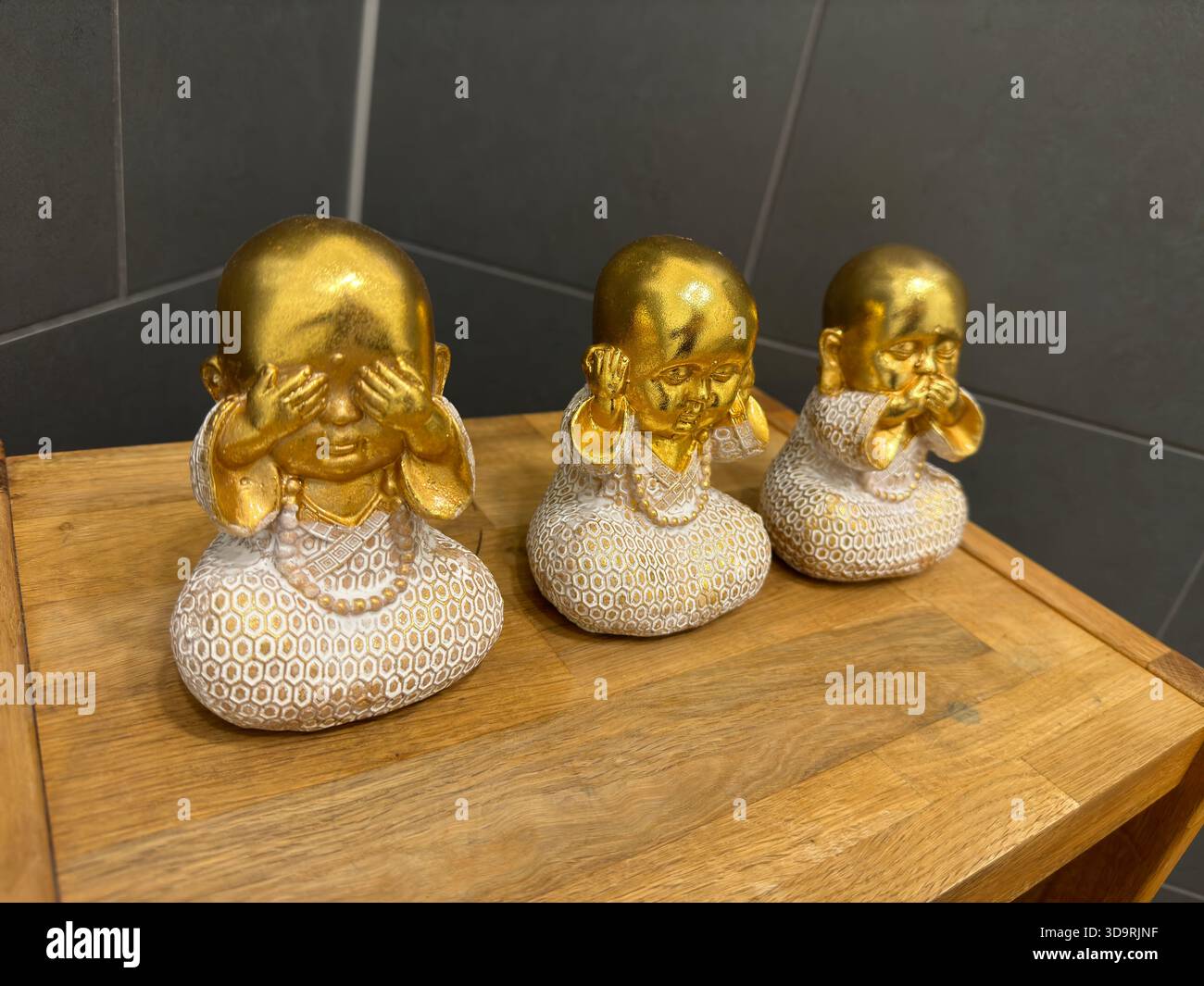 A wooden cabinet holds three small golden Chinese statues representing ...