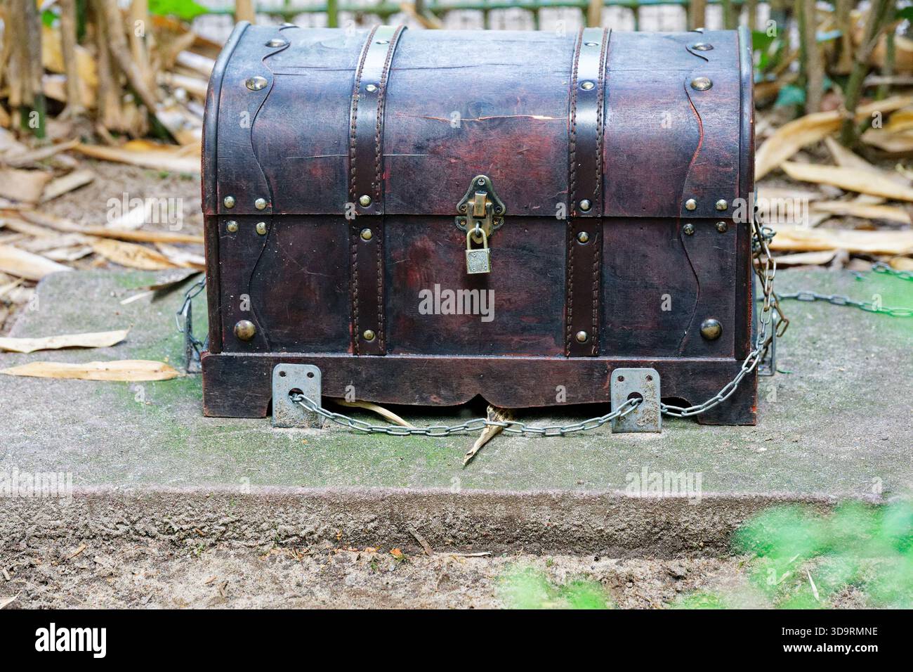 A secured wooden treasure chest rests on a concrete platform. Chains ...