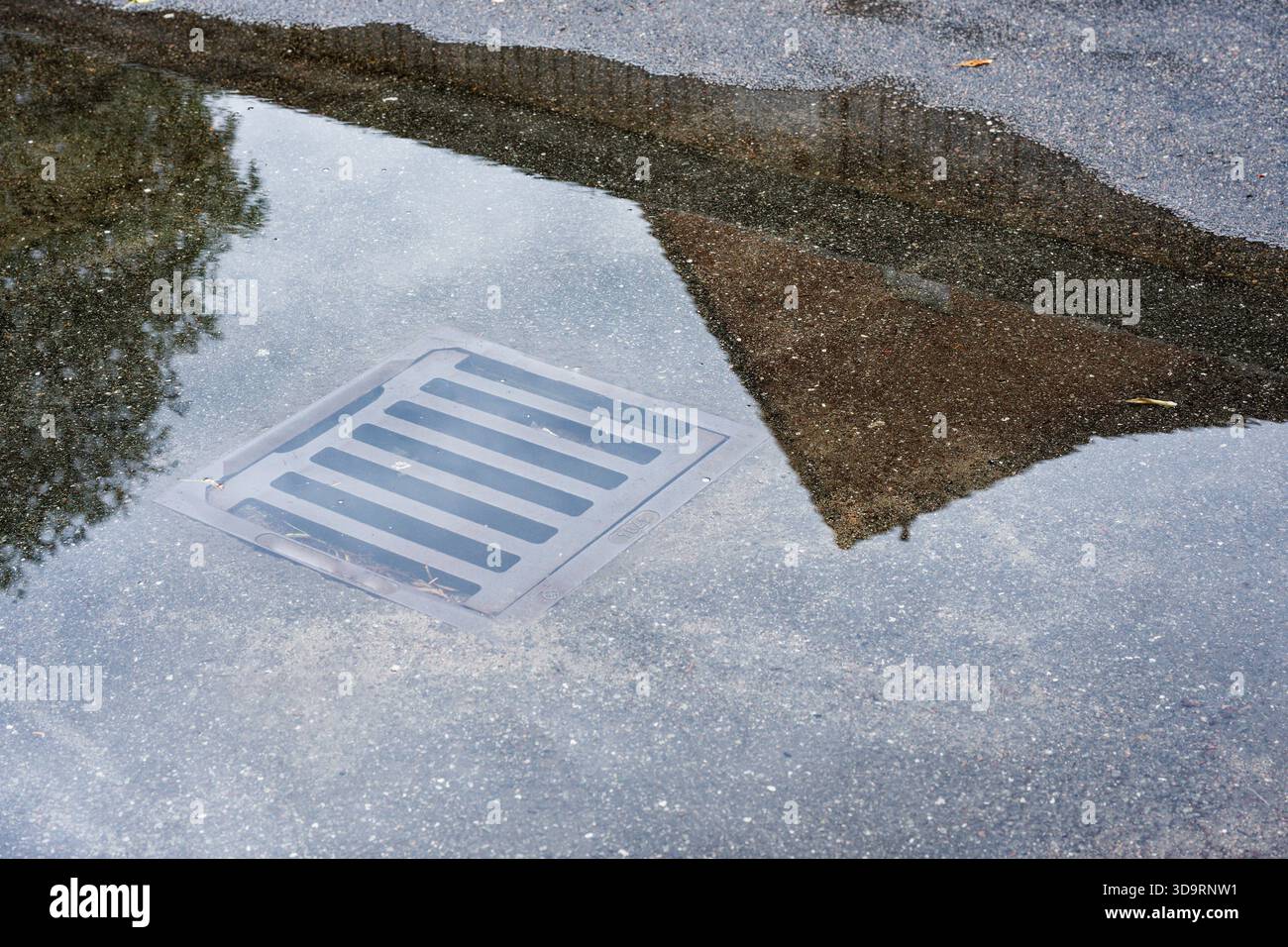 A thin sheet of rainwater covers the gutter grate so that only faint ...