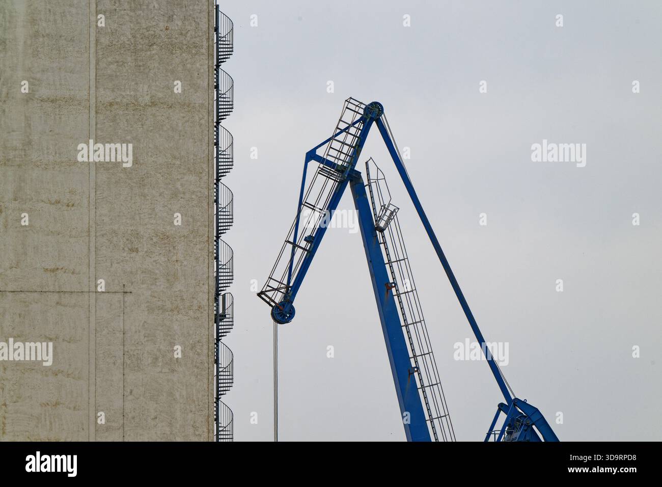 A deep blue crane stands by a towering concrete structure. Curved ...