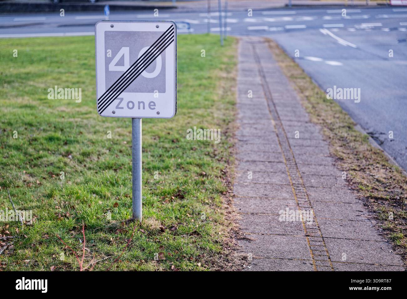 A short roadside sign sits on the grass beside the sidewalk showing the ...