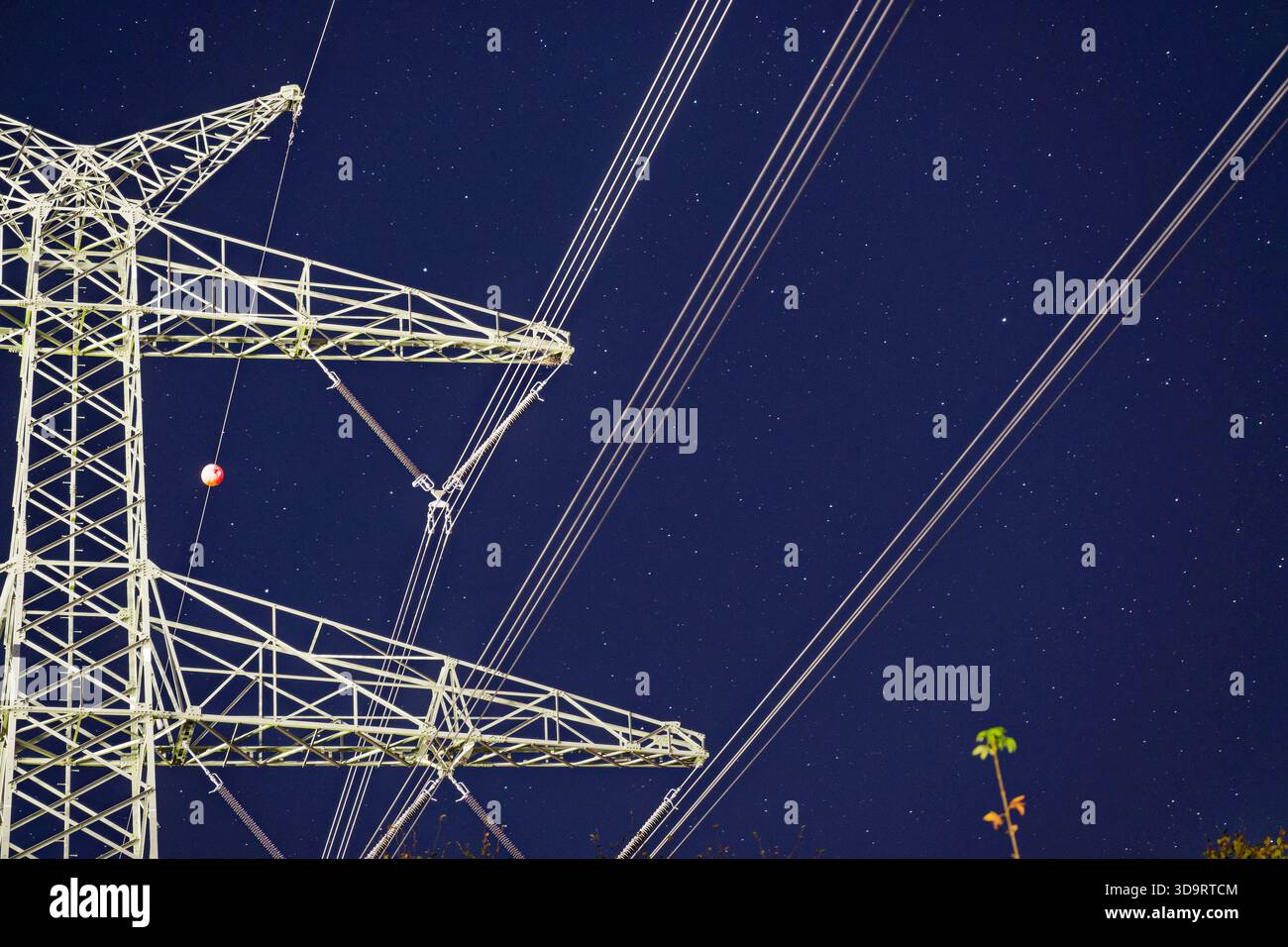 Bright points scatter across deep night as transmission lines stride ...