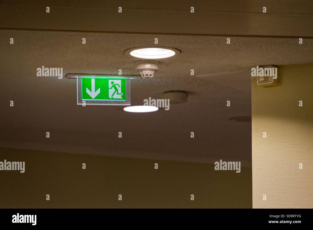 A round smoke detector sits on the ceiling near an emergency exit sign ...