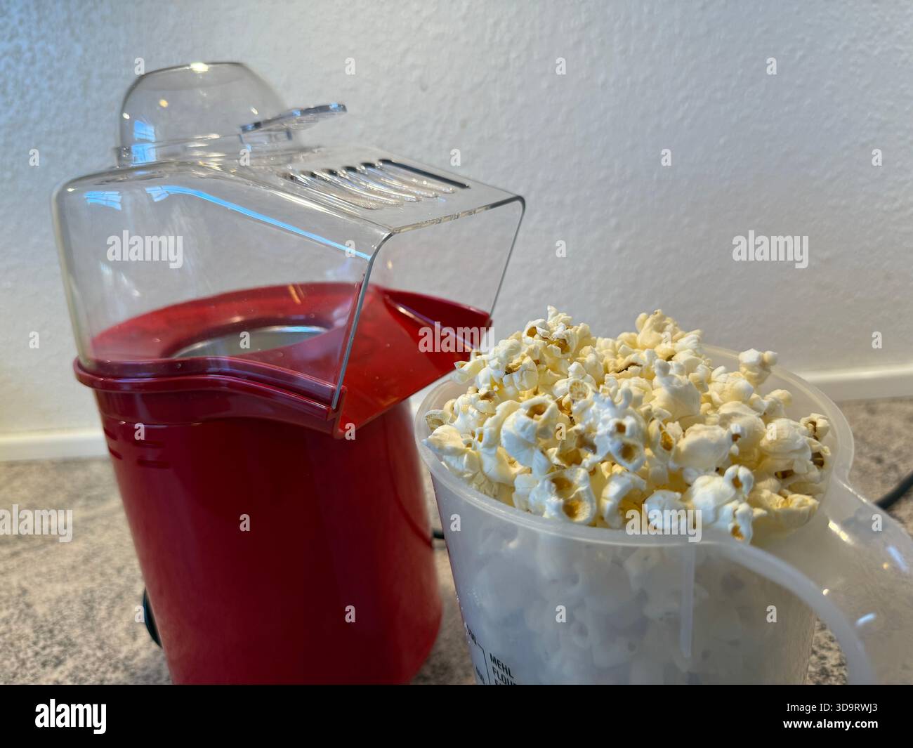 A hot air popcorn maker stands beside a full measuring cup of freshly ...