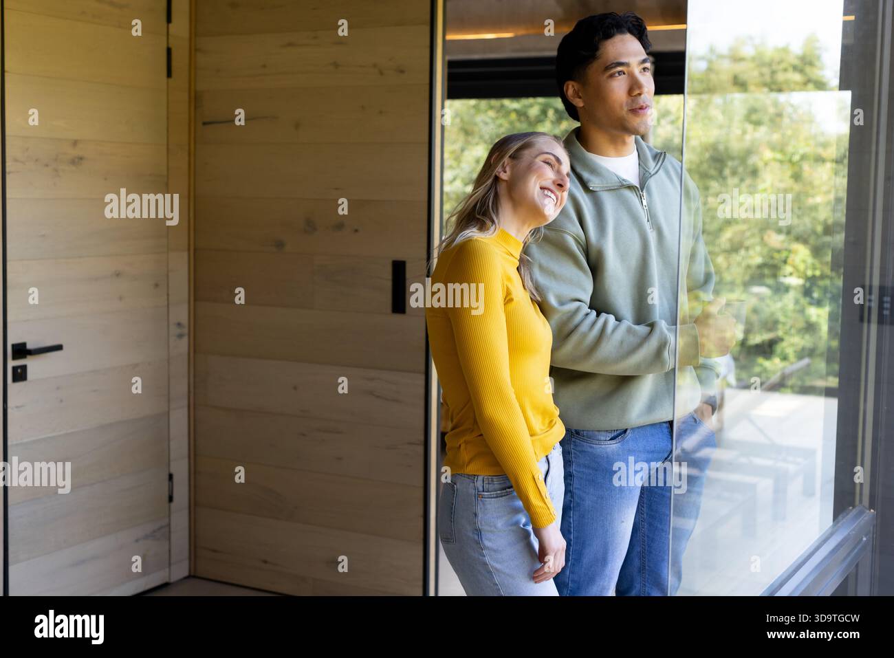 Diverse couple gazing through glass sliding door in cabin with wooden ...