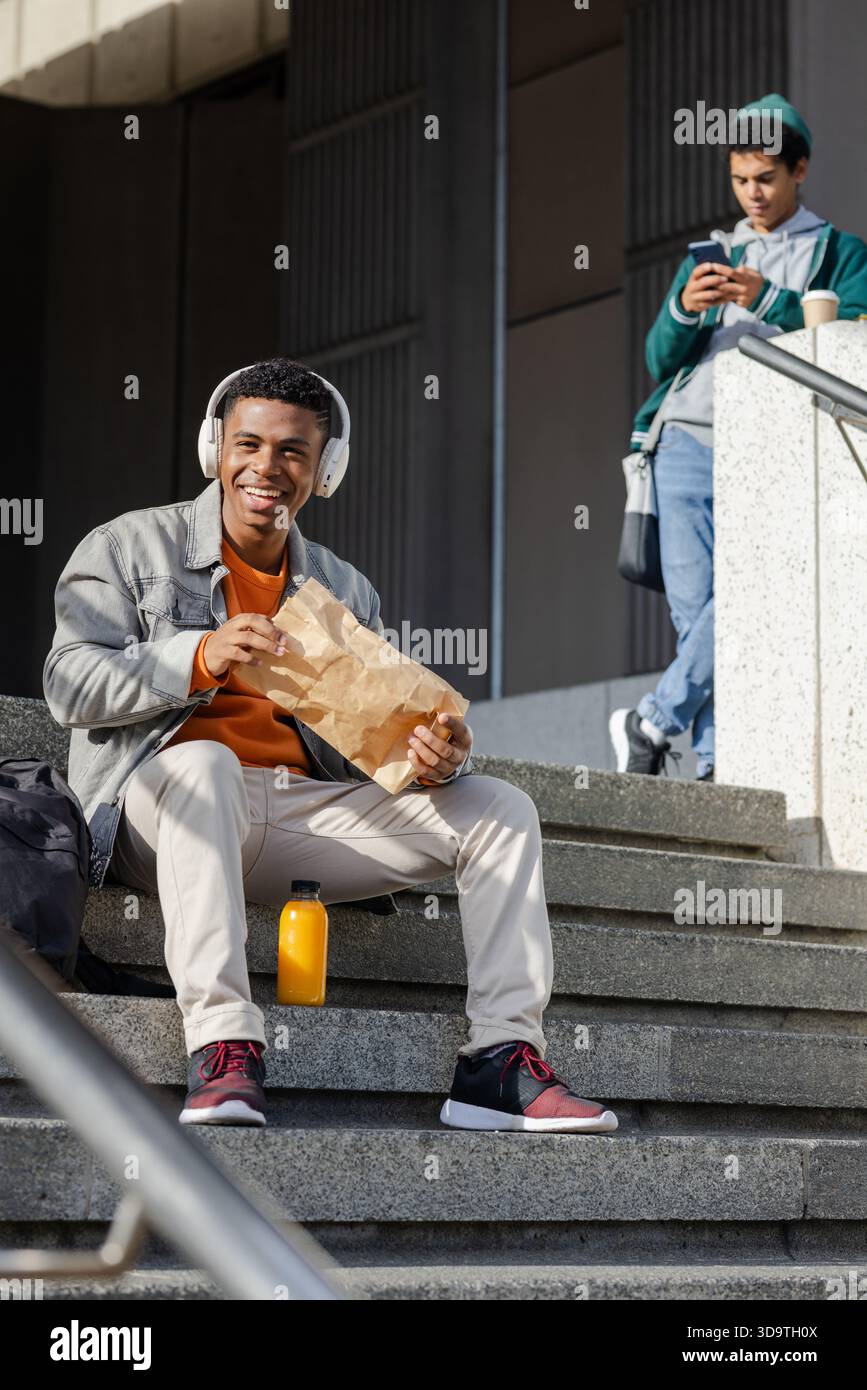 African American classmates sitting campus steps eating from paper bag ...