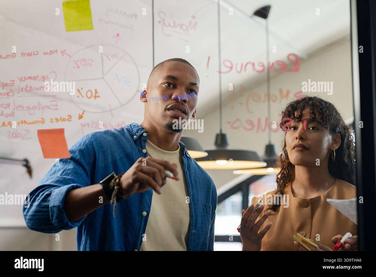 African American coworkers drawing diagrams on glass writing panel in ...