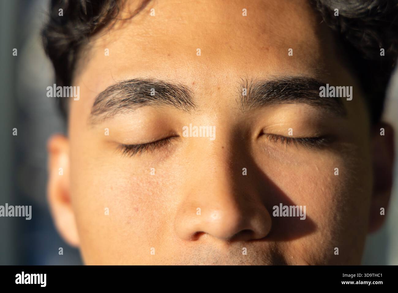 Asian man basking in warm sunlight falling across face near window with ...
