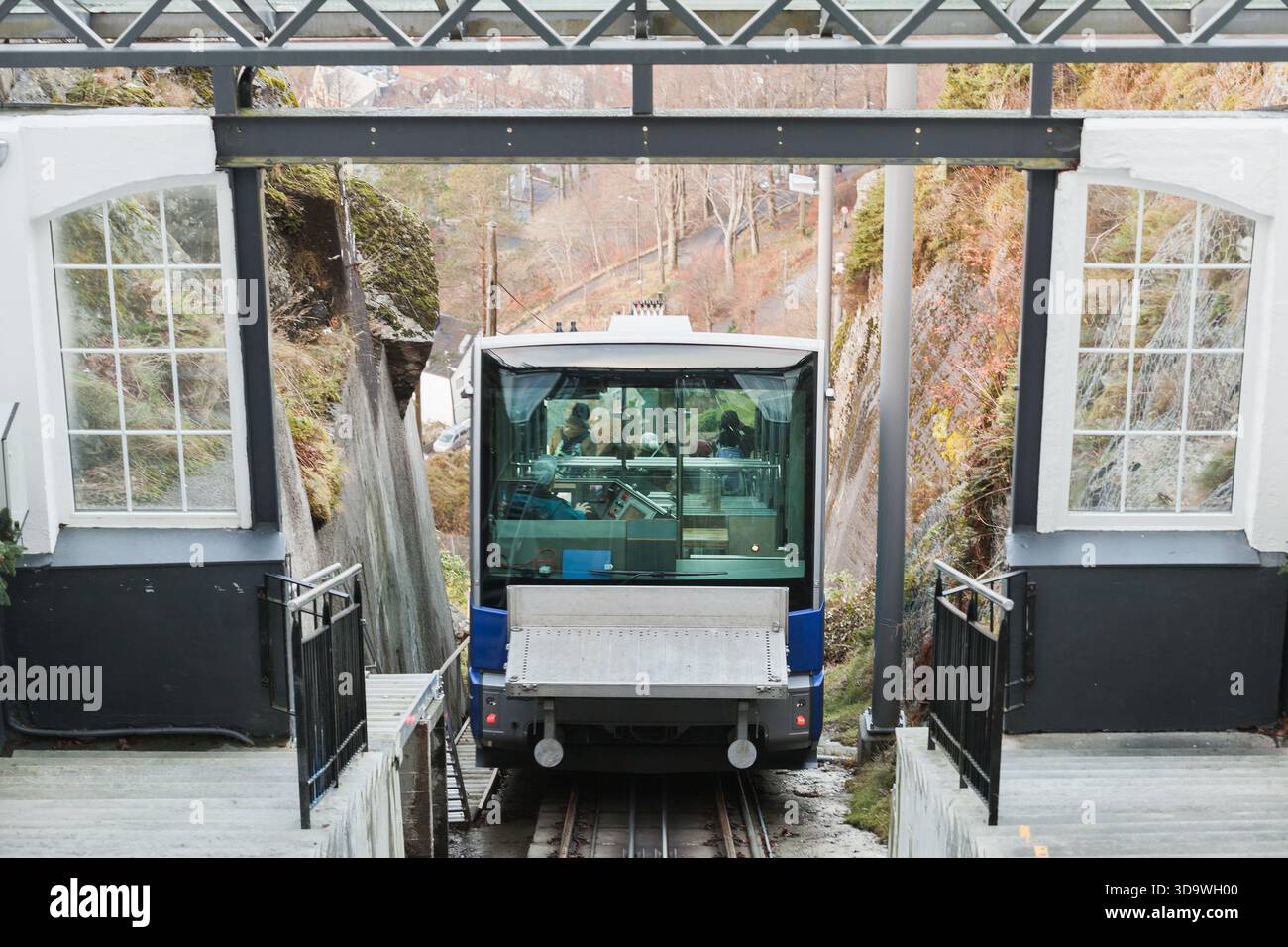 A modern cable car enters a glass-walled station, passengers visible ...