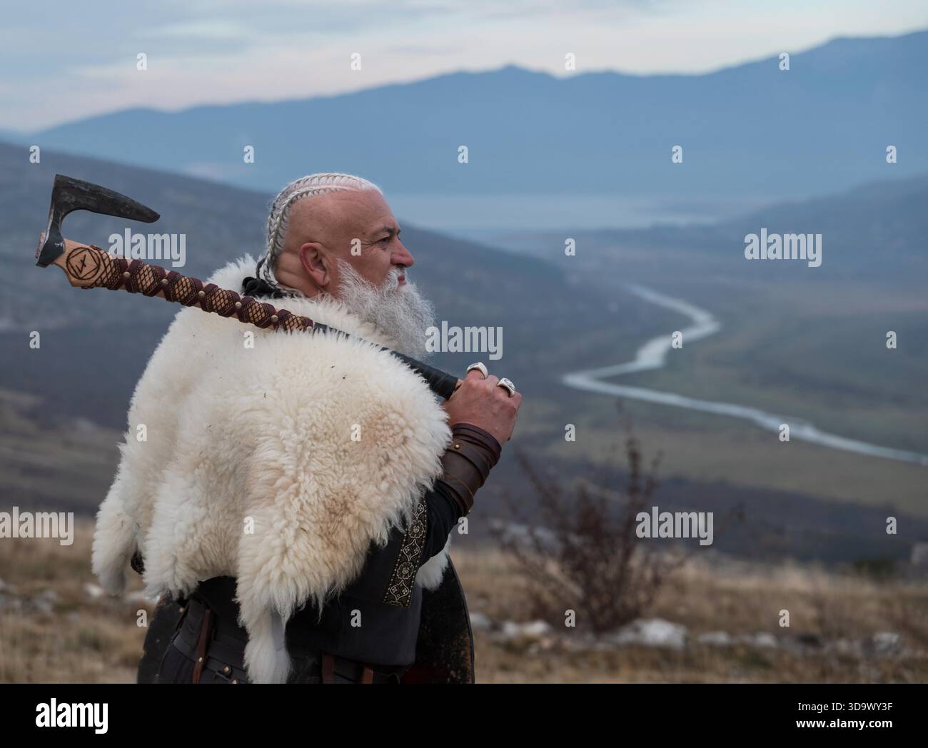 Viking warrior with axe standing on mountain cliff, wearing fur cloak ...