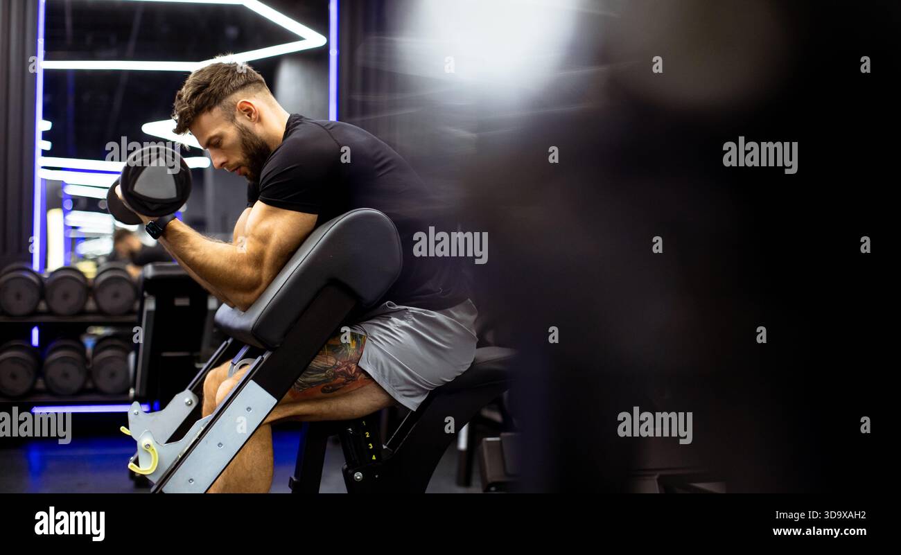 A strong man with tattoos works out in a sleek gym. He focuses on ...
