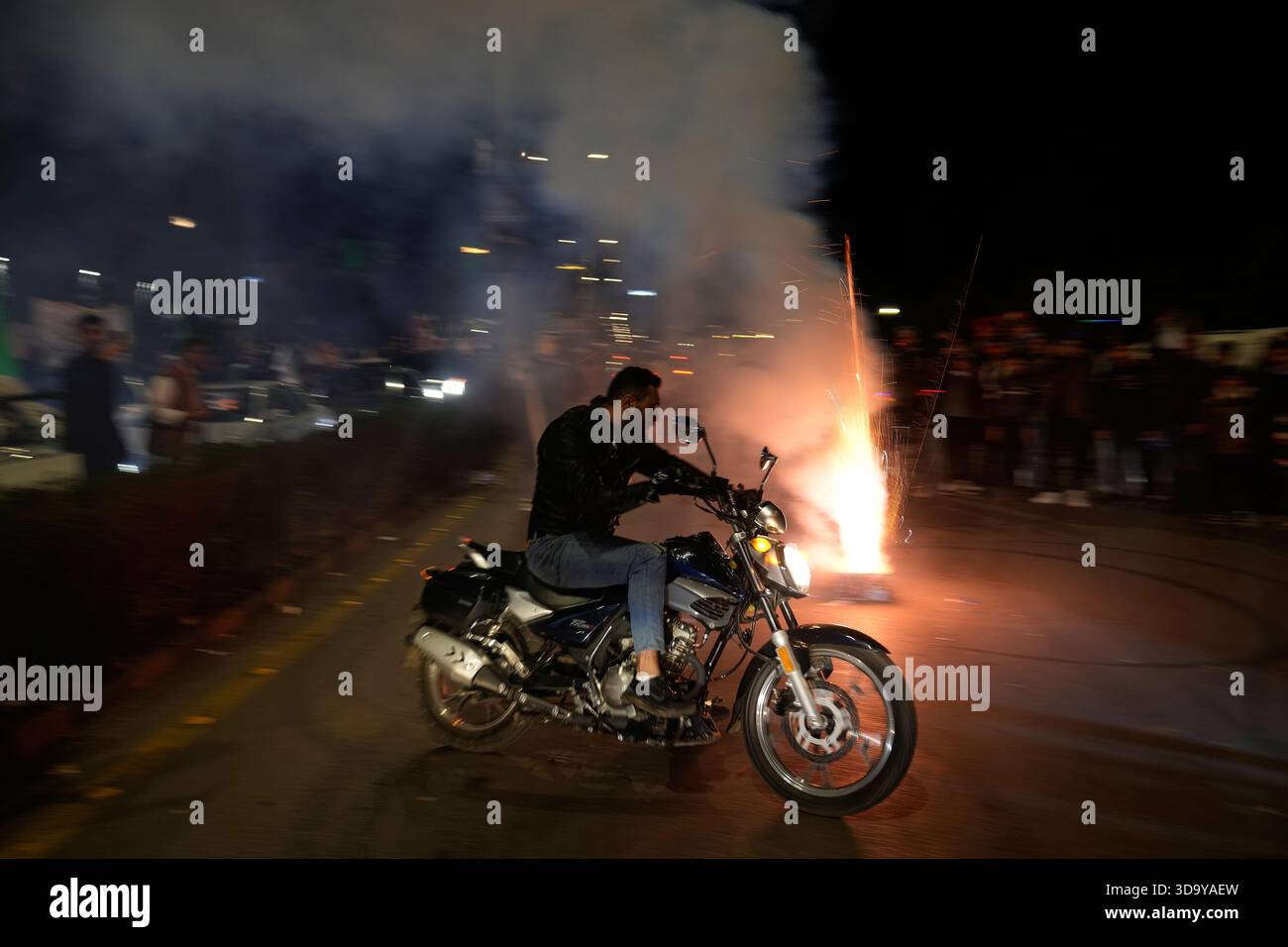 A Syrian man rides his motorcycle as others explode fire fireworks ...