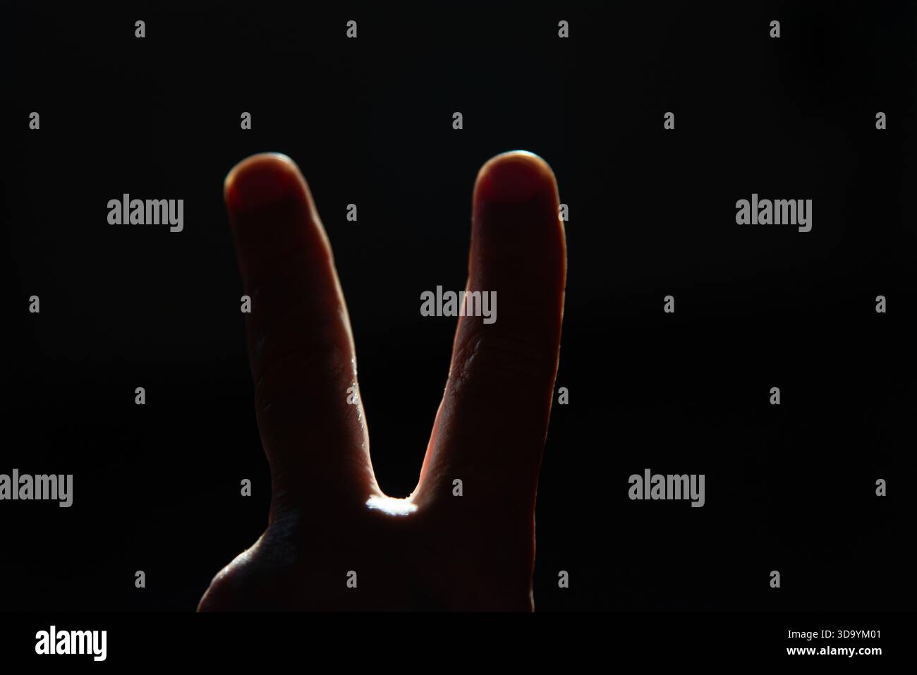 Hand in backlight making the two-finger sign, peace or victory, against ...