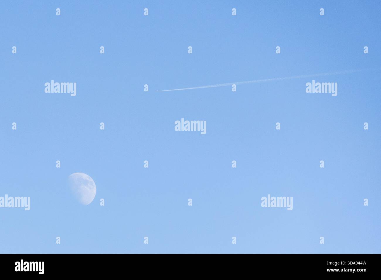 Half moon visible in the daytime sky with an airplane contrail flying ...