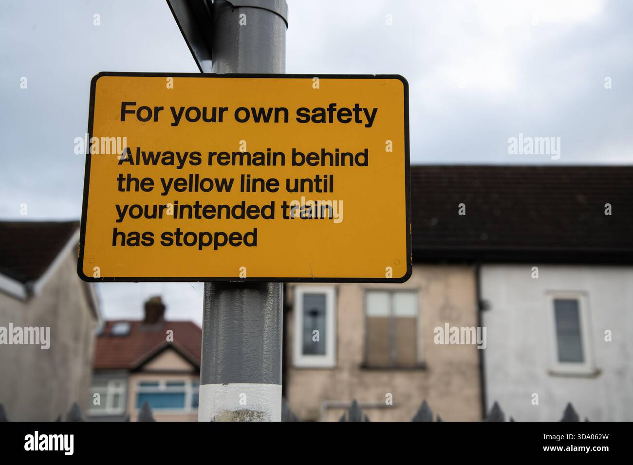A yellow safety sign on a railway platform advising passengers to ...