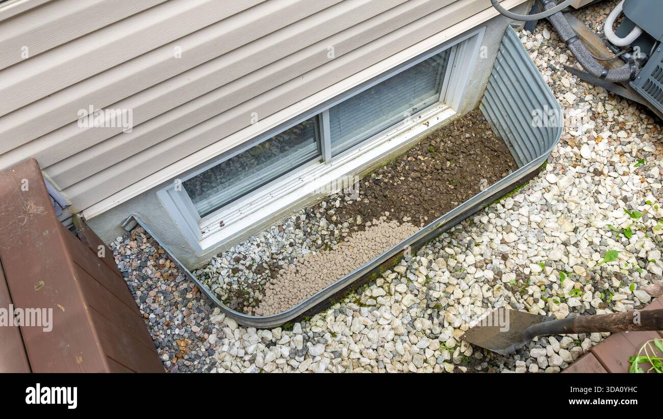 Gravel and soil are arranged around a basement window, highlighting ...