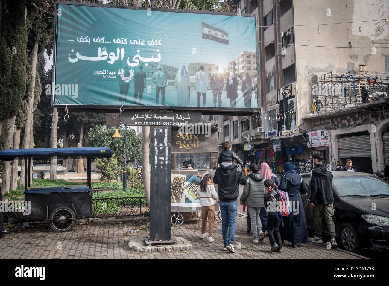 A family walk under a billboard in central Homs. Celebrations were held ...