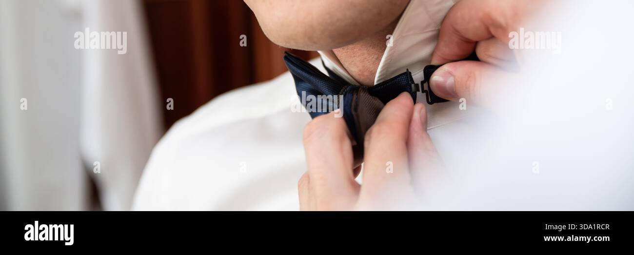 The best man helps the groom fasten his bow tie. A close-up of a ...