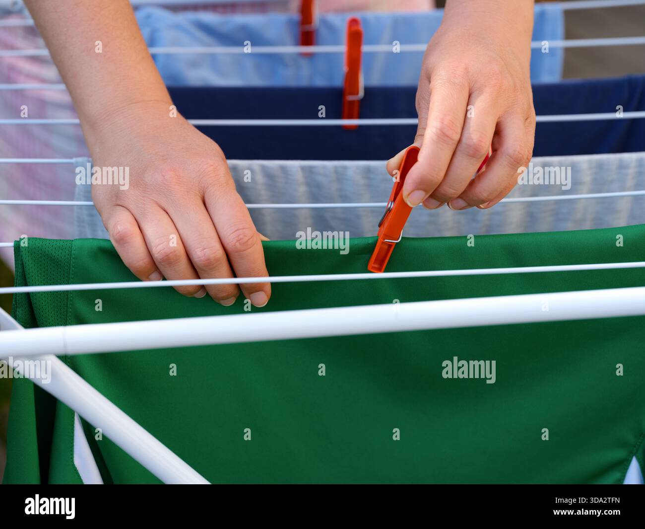 Woman hands using a clothespin to hang up laundry to dry on a drying ...
