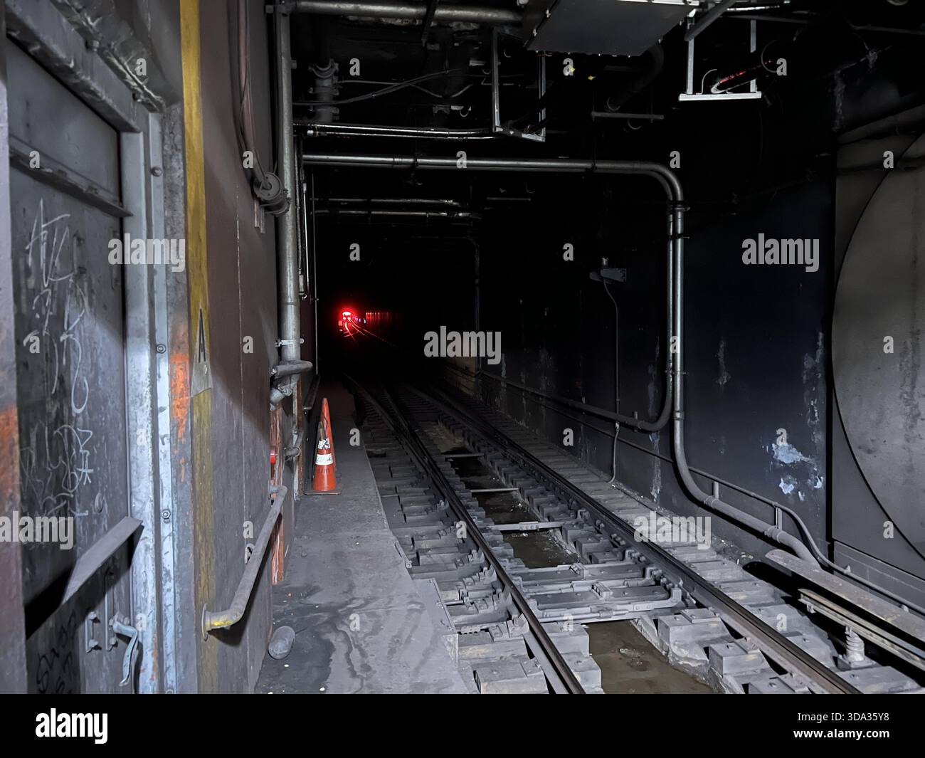 BART tunnel with maintenance walkway, utility pipes, and distant red ...