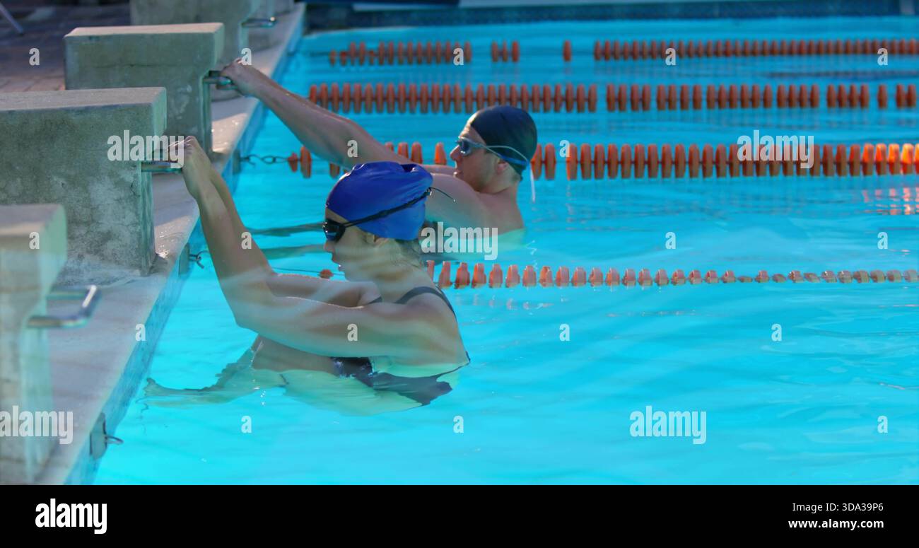 Gripping starting handles, two swimmers bracing at pool wall outdoors ...