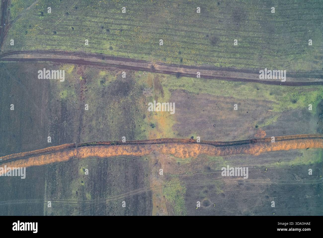 Aerial drone shot of a fresh infantry trench dug in a green field next ...