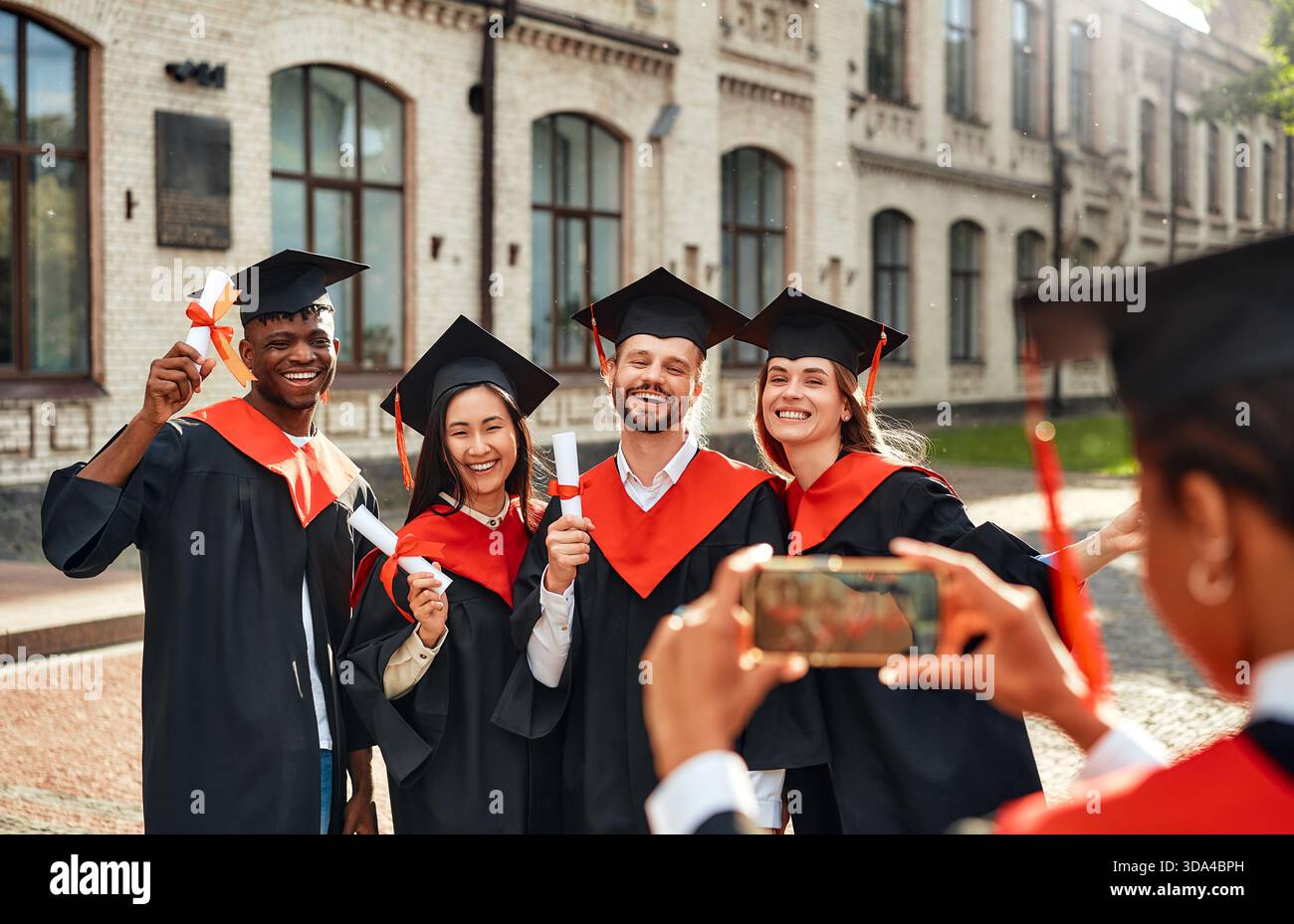 Diverse graduates in caps and gowns celebrate happily outside a ...