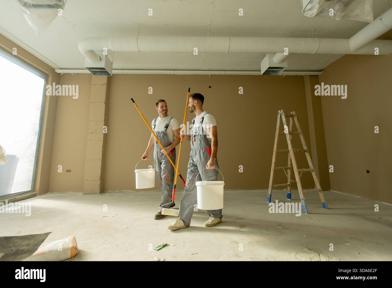 Two men in overalls carry paint buckets and long brushes in a newly ...