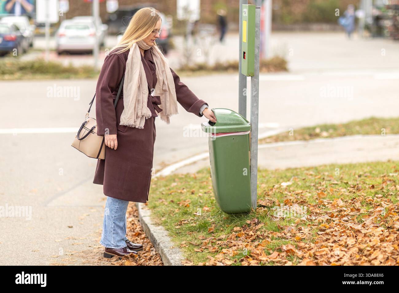 Woman throws trash into a public outdoor bin in autumn, wearing coat ...