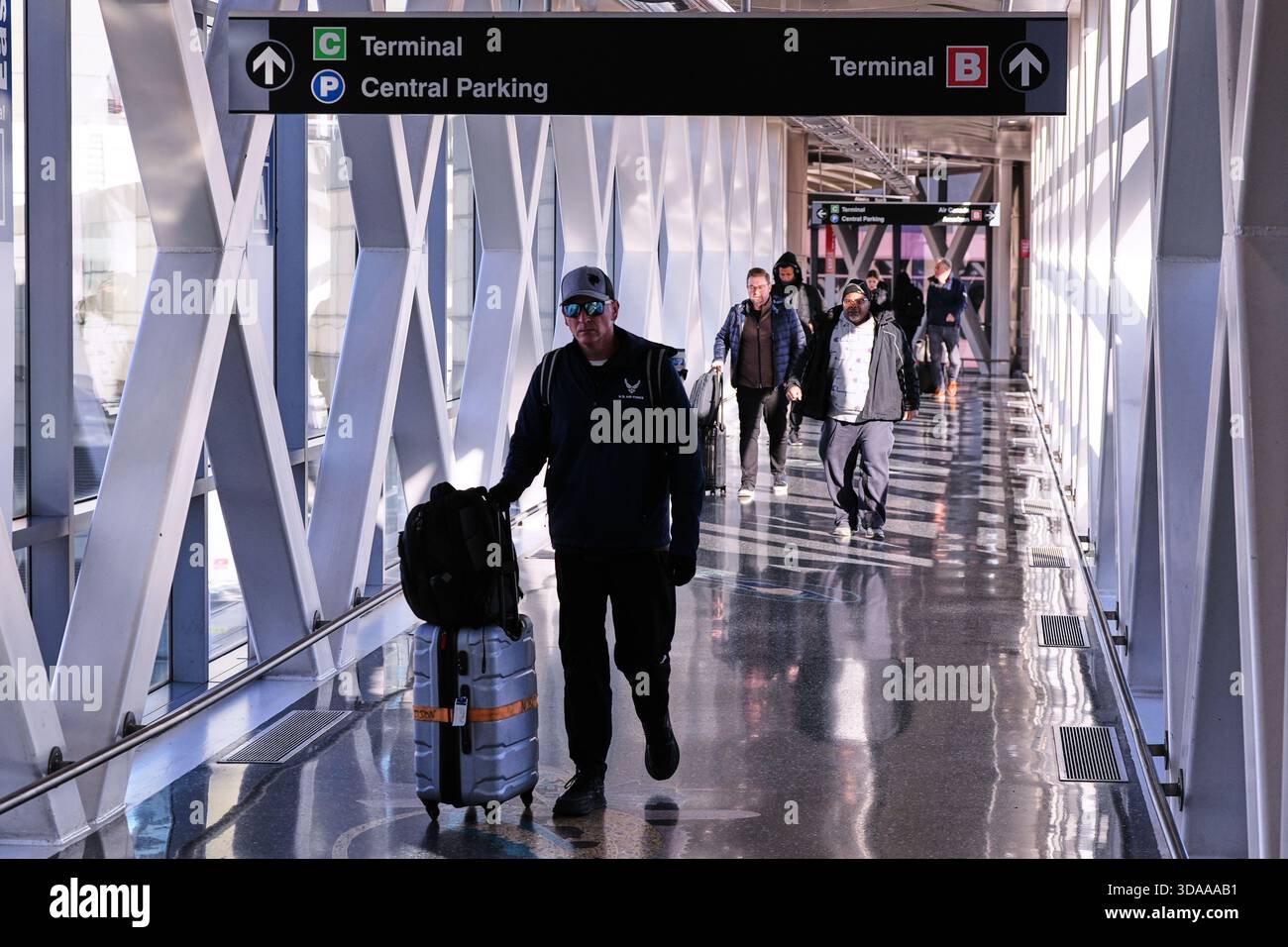 Travelers roll their luggage through a sky bridge at Terminal A at ...