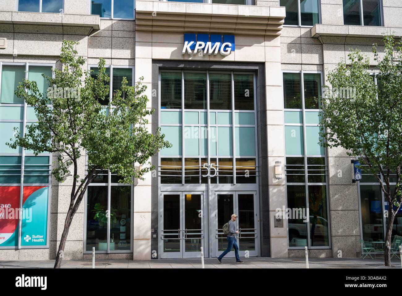 A person walks past the facade of KPMG office with sign and logo ...