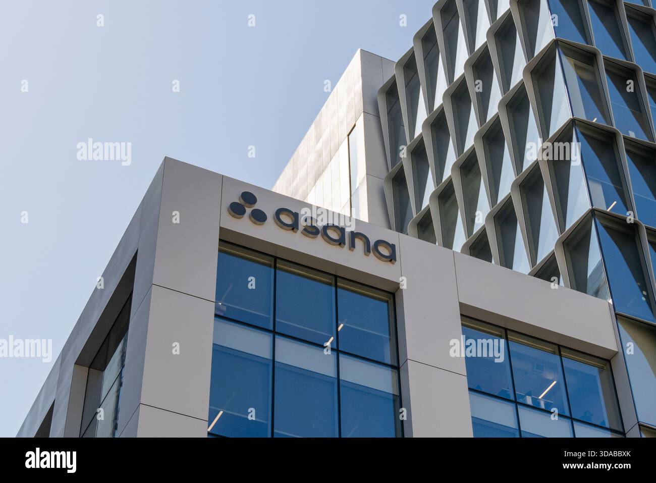 Low-angle view of Asana office building with logo and geometric glass ...